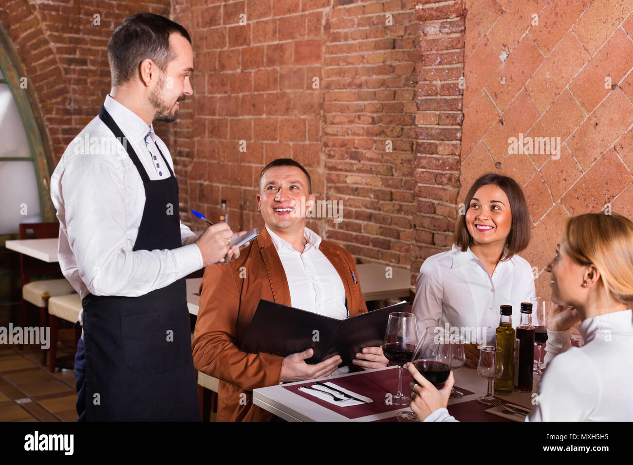 Diligent smiling male waiter taking order from visitors in country ...