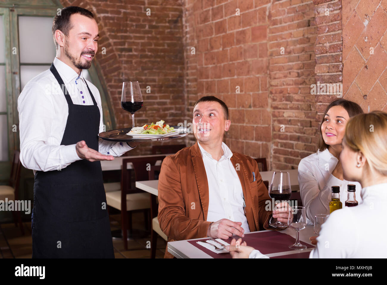 positive waiter placing order in front of guests in country restaurant ...
