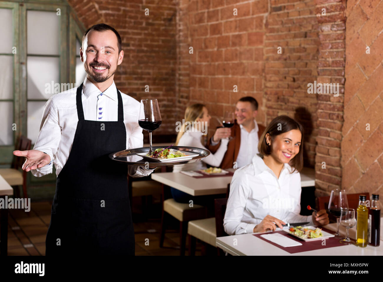 Positive male waiter showing country restaurant to visitors Stock Photo ...