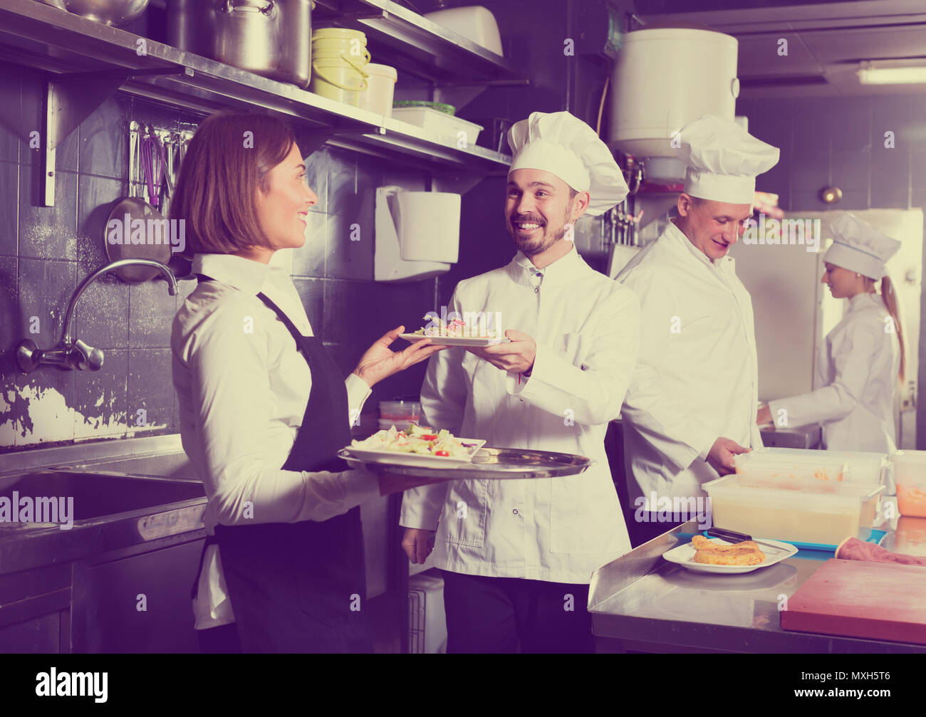 Adult female waiter taking ordered dishes from restaurant’s kitchen ...