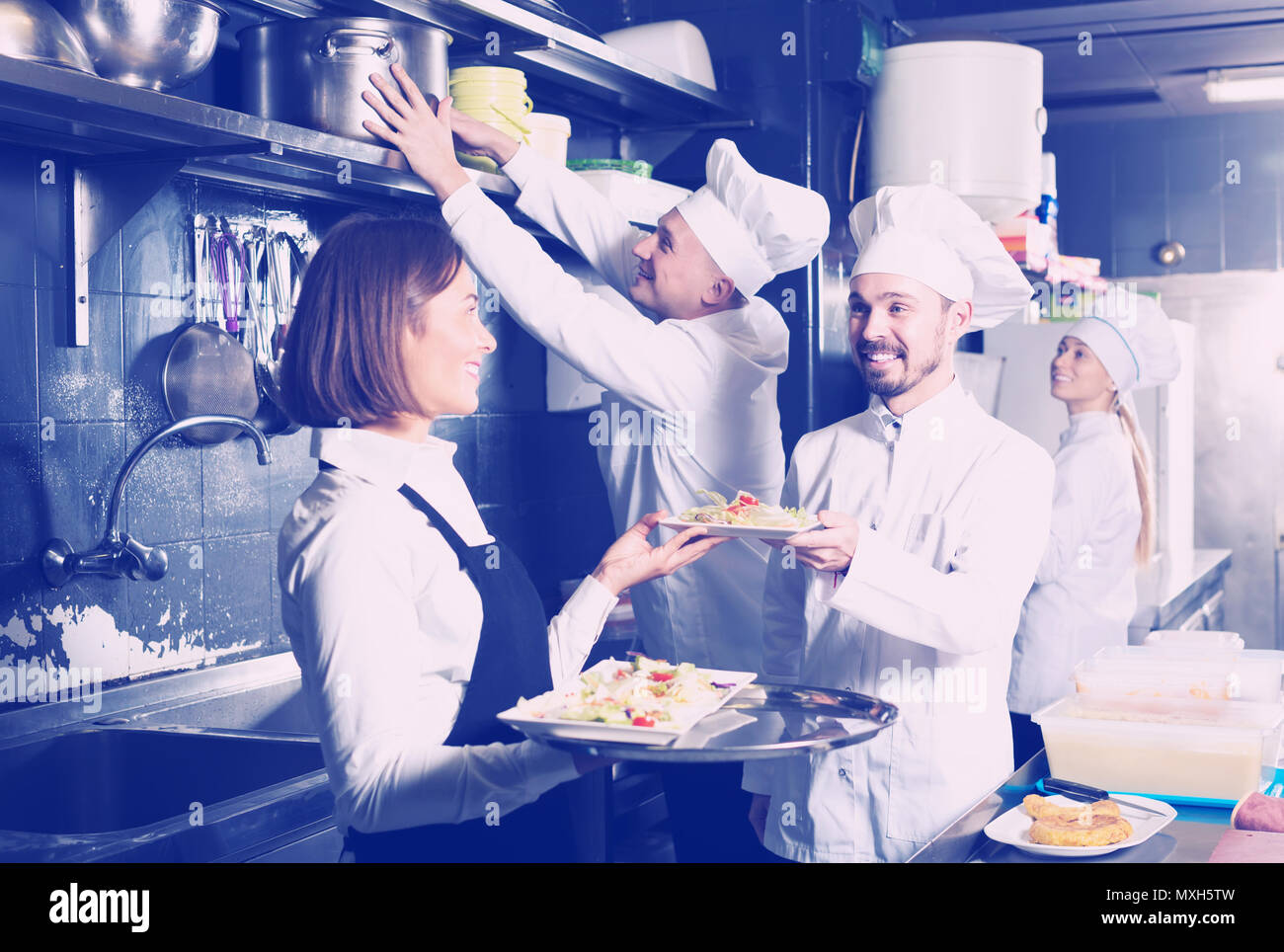 Cheerful female waiter taking order of meal from restaurant’s kitchen ...