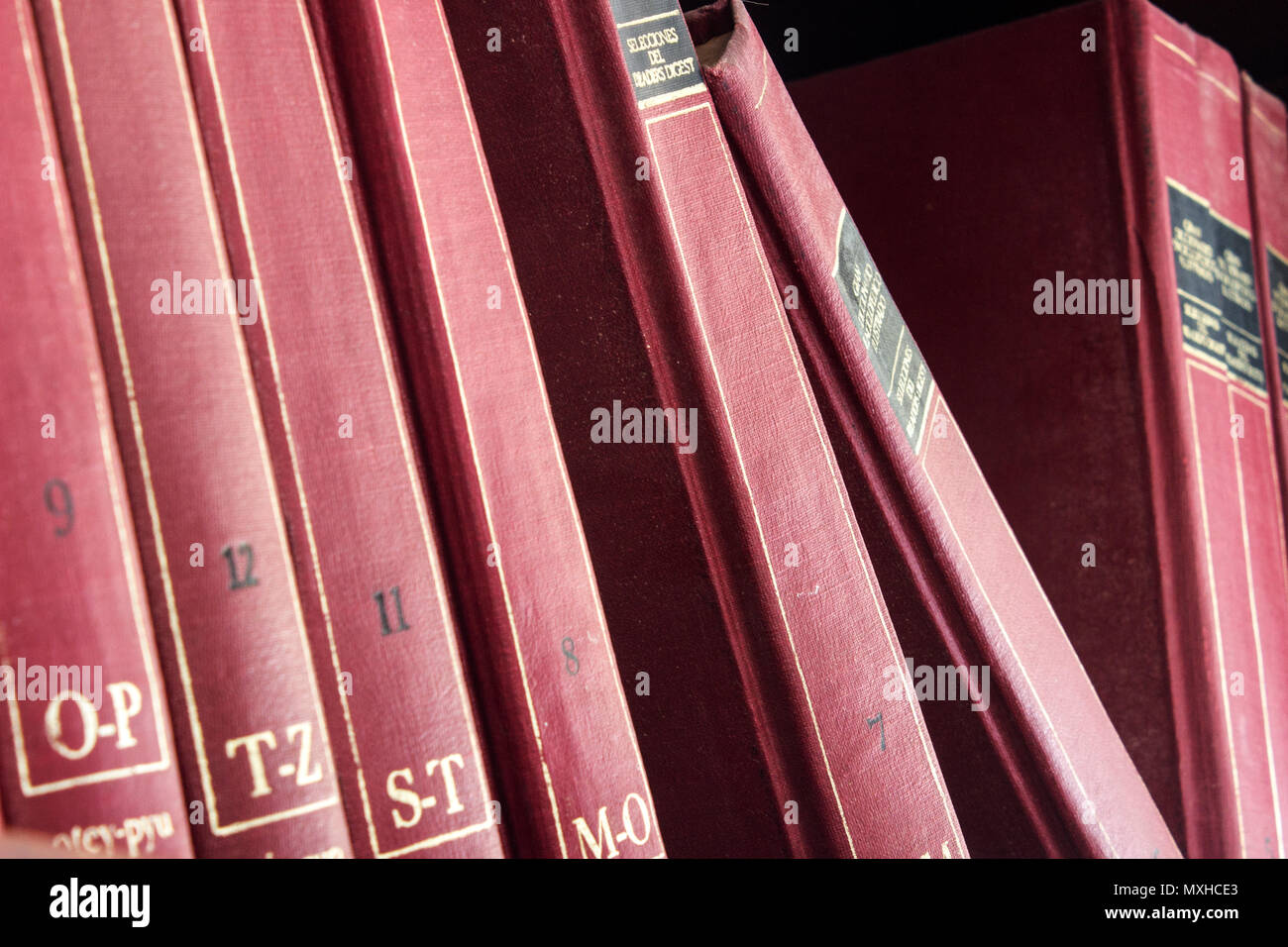 An old red encyclopedia collection standing in a dust covered shelf ...