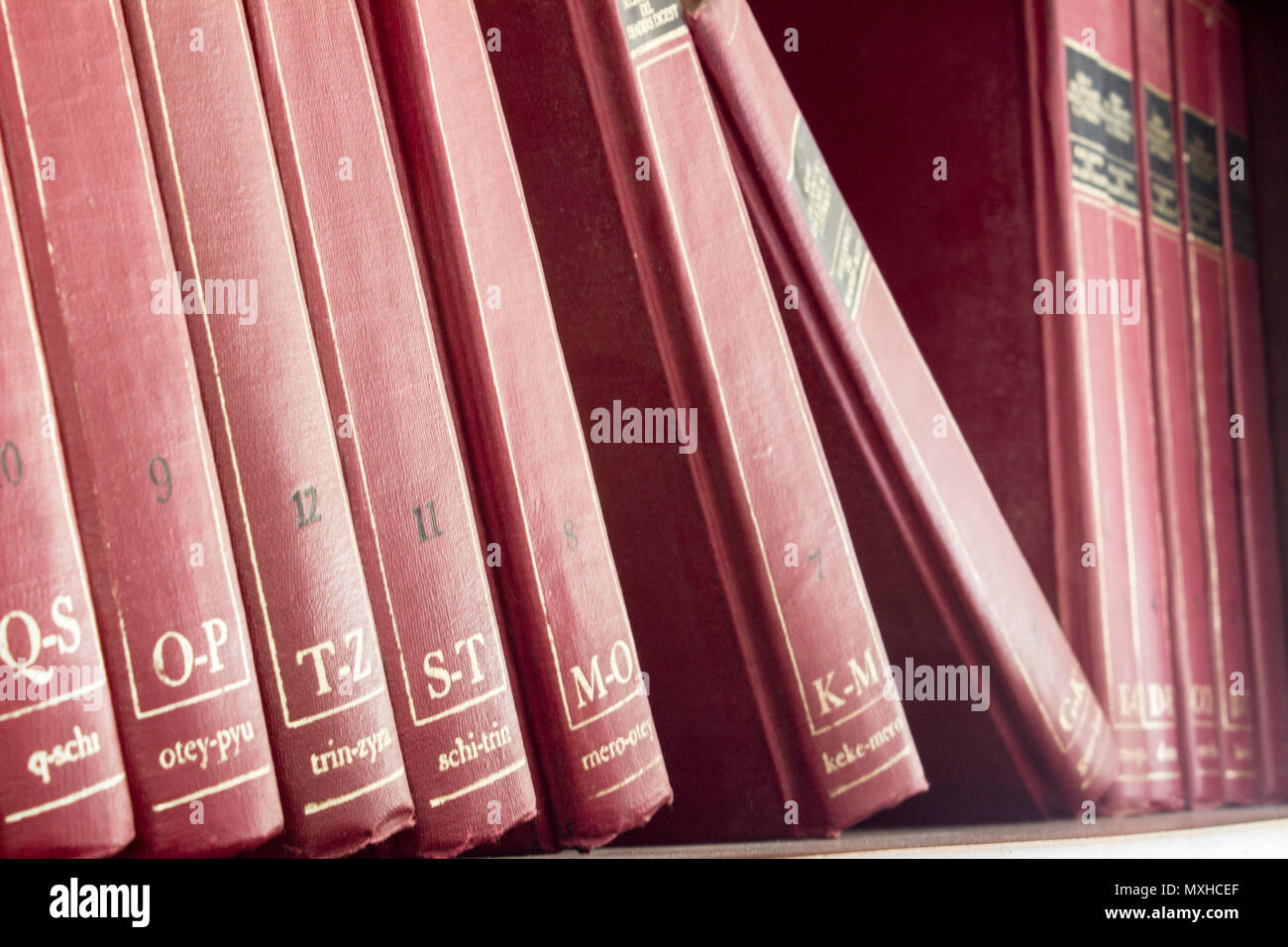 An old red encyclopedia collection standing in a dust covered shelf ...