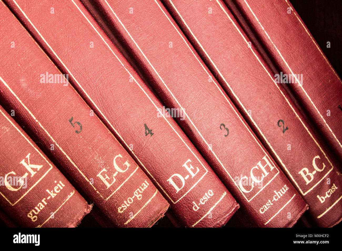 An old red encyclopedia collection standing in a dust covered shelf ...