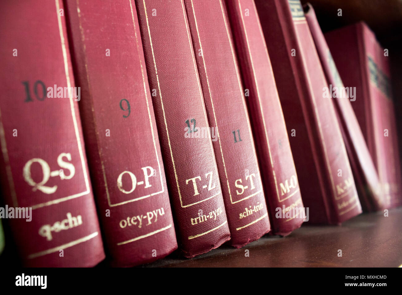 An old red encyclopedia collection standing in a dust covered shelf ...