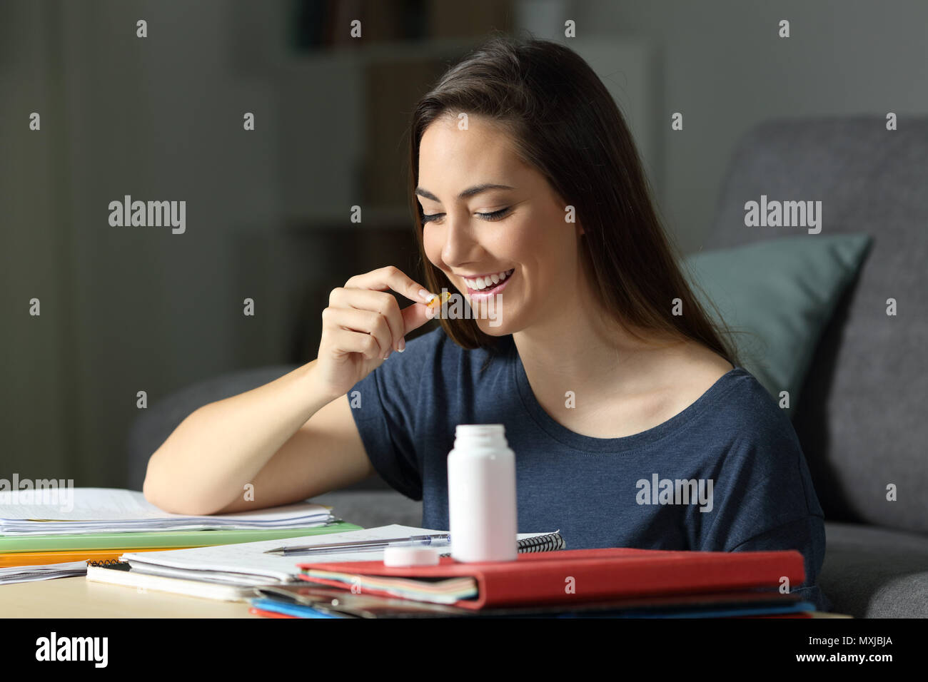 Happy student studying late hours in the night taking a vitamin pill at ...