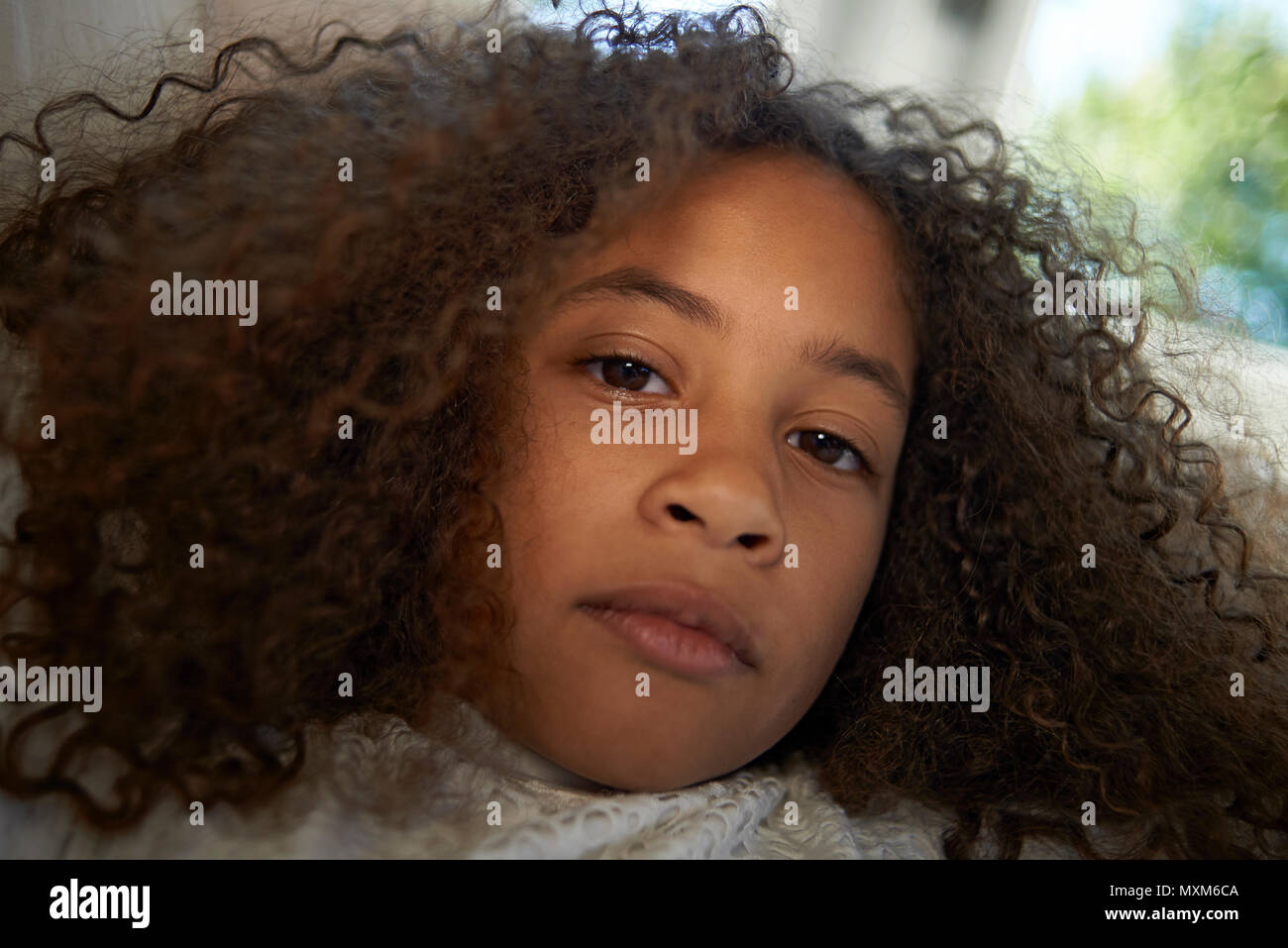 Portrait of a young preteen mixed race girl with big curly hair looking ...