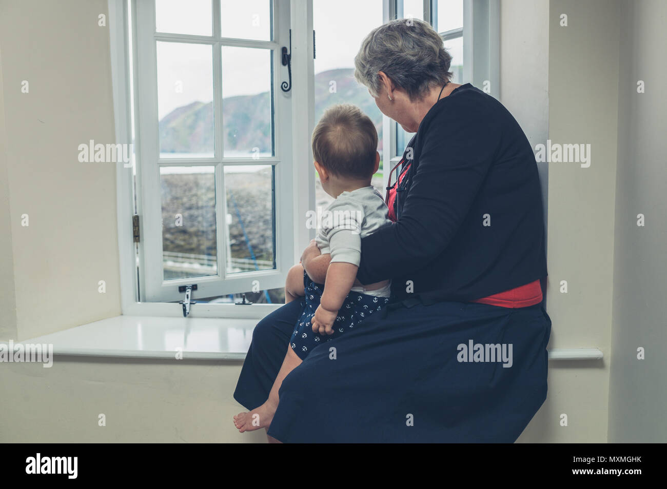 A grandmother is sitting with her grandchild by the window of a rural ...