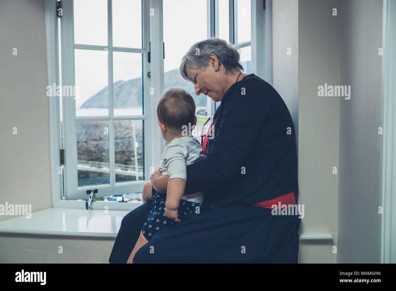 A grandmother is sitting with her grandchild by the window of a rural ...