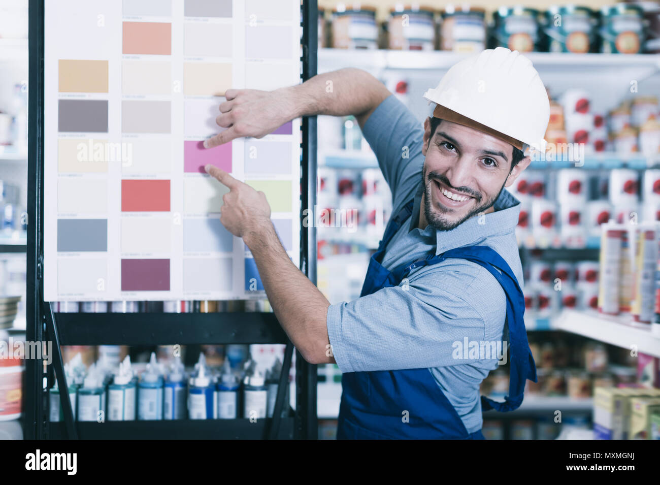 Smiling foreman in blue overalls showing samples of paint on stand in ...