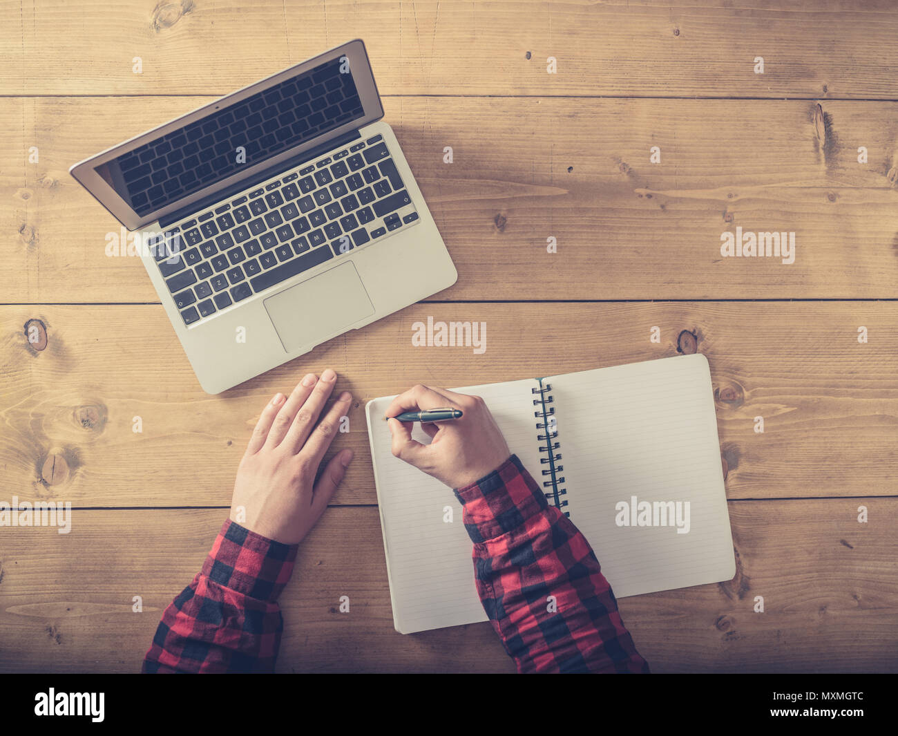 Overhead shot of a man writing in a notepad with a laptop next to him ...