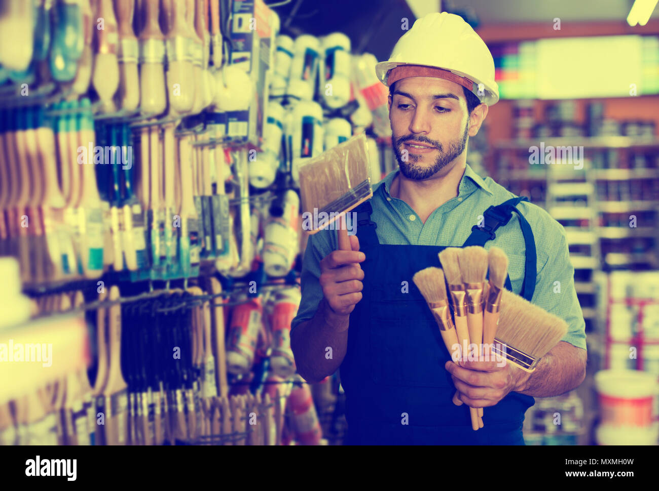 Happy workman standing amongst racks in paint store selecting brushes ...