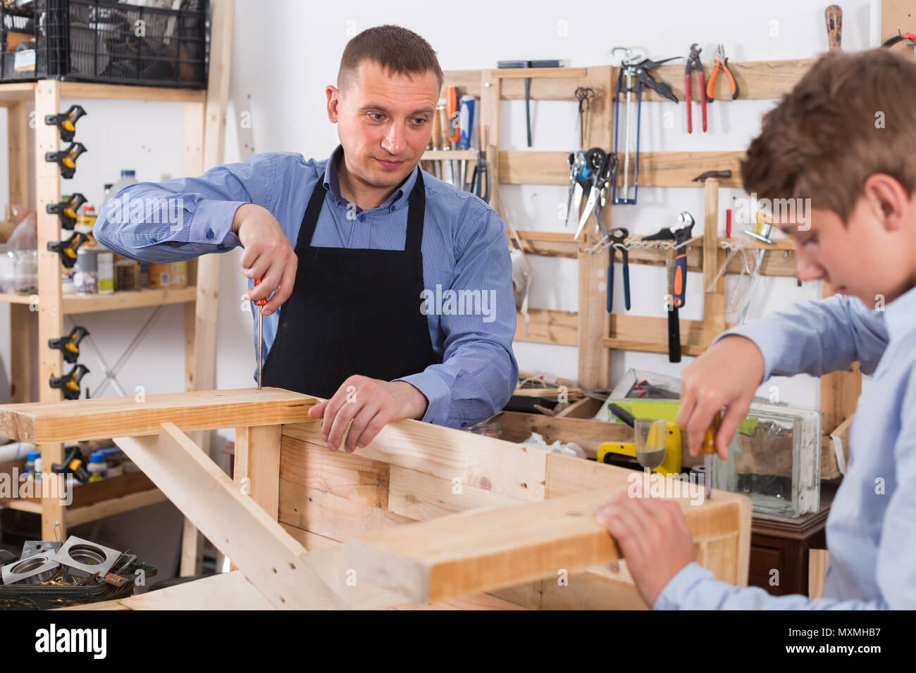 happy european teacher and boy chiselling a wooden bench in workshop ...