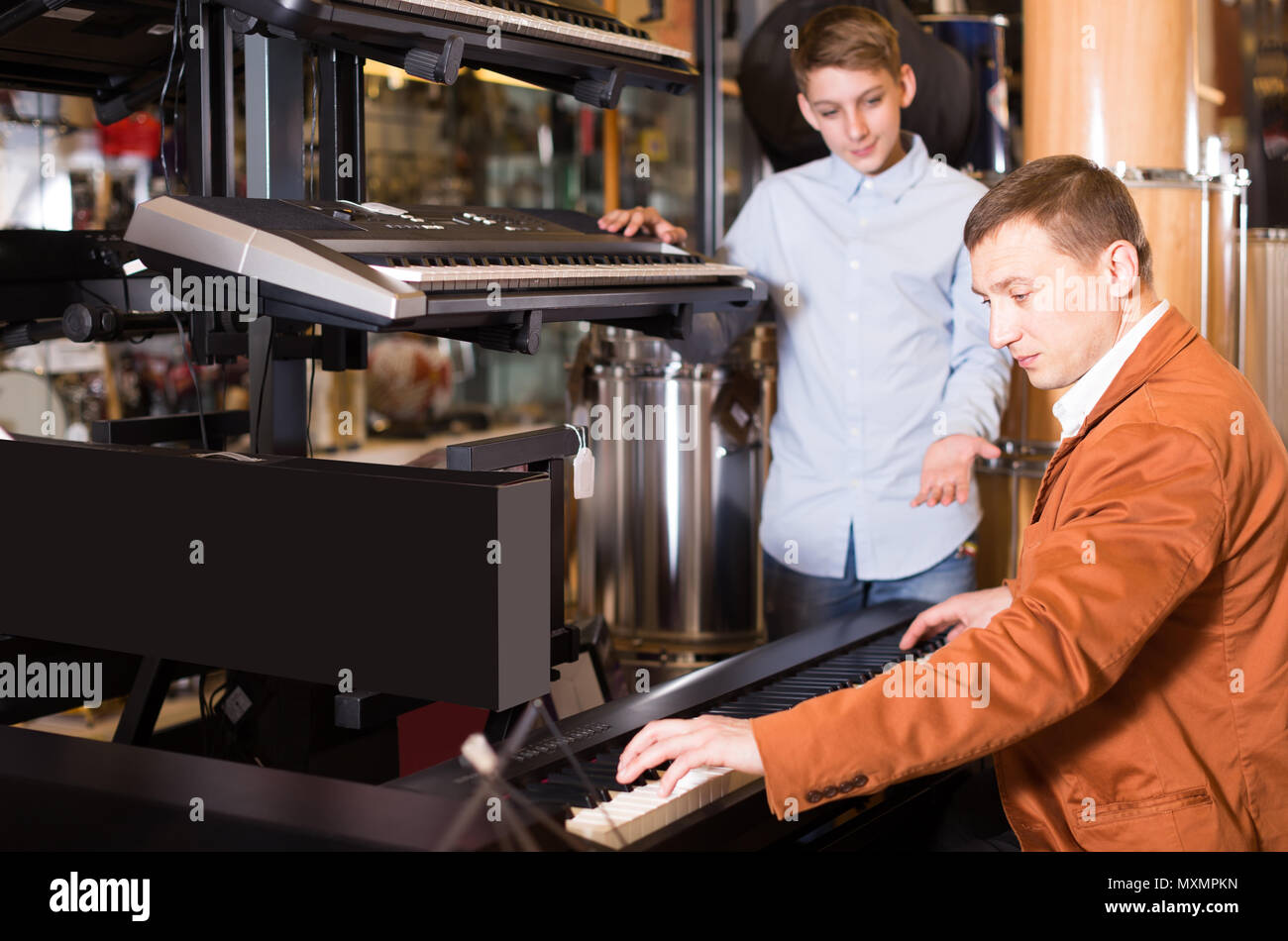 Father demonstrates his son playing a synthesizer in a music store ...
