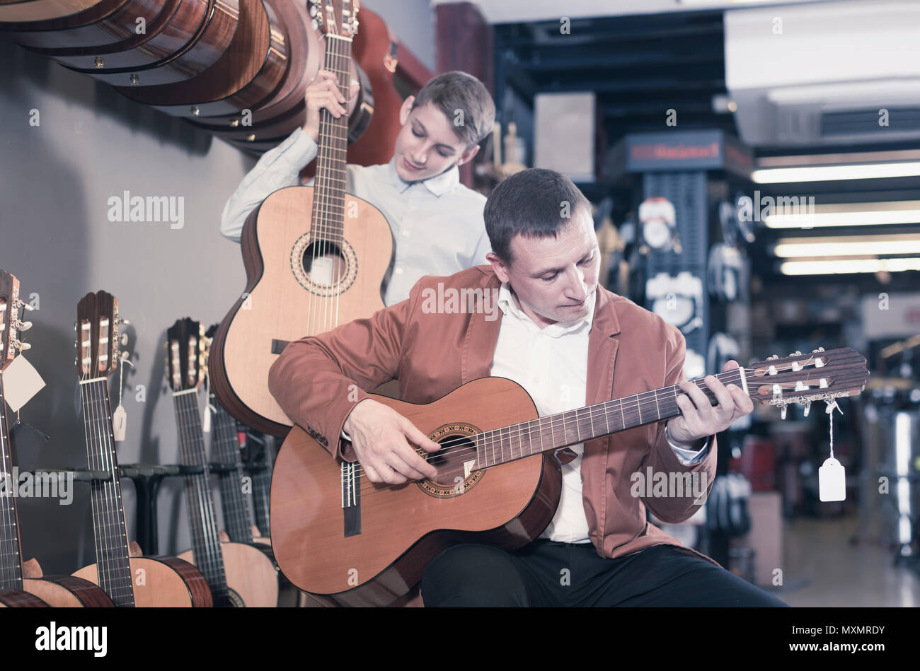Teenager boy and father are searching acoustic guitar in a music store ...