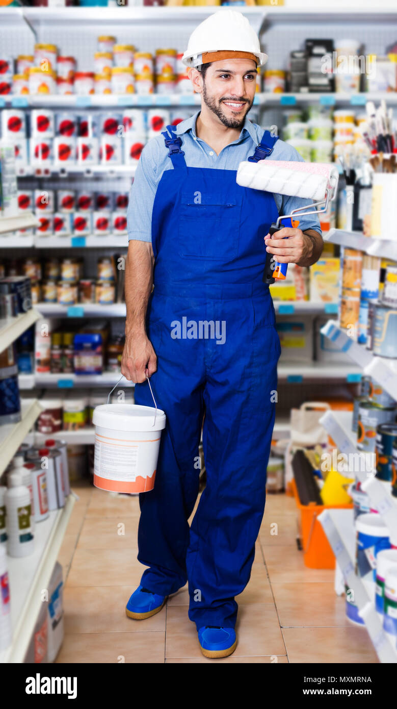 Laughing workman in blue overalls with paint and brushes in hands in ...