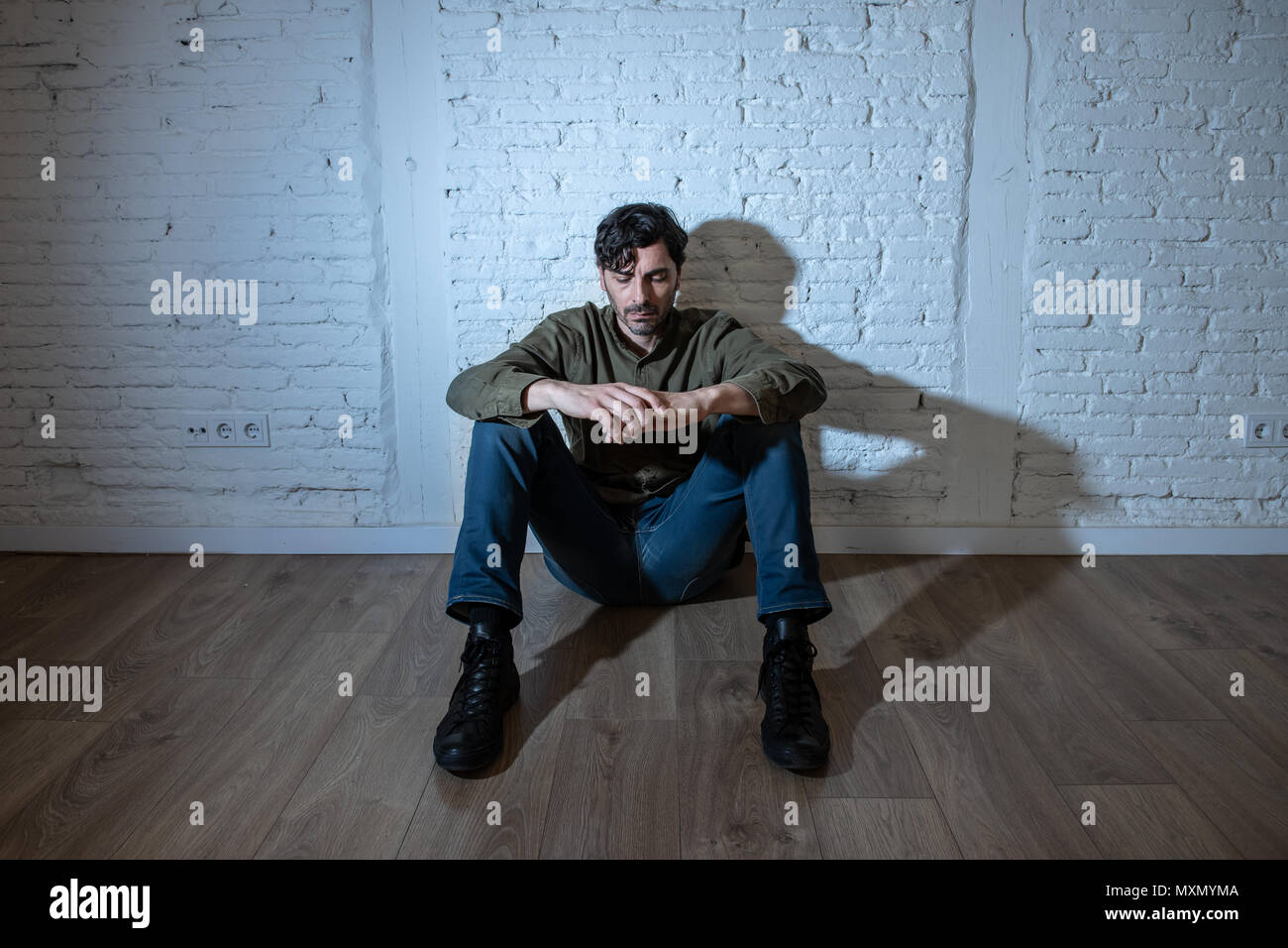 young depressed man sitting against a white wall at home with a shadow ...