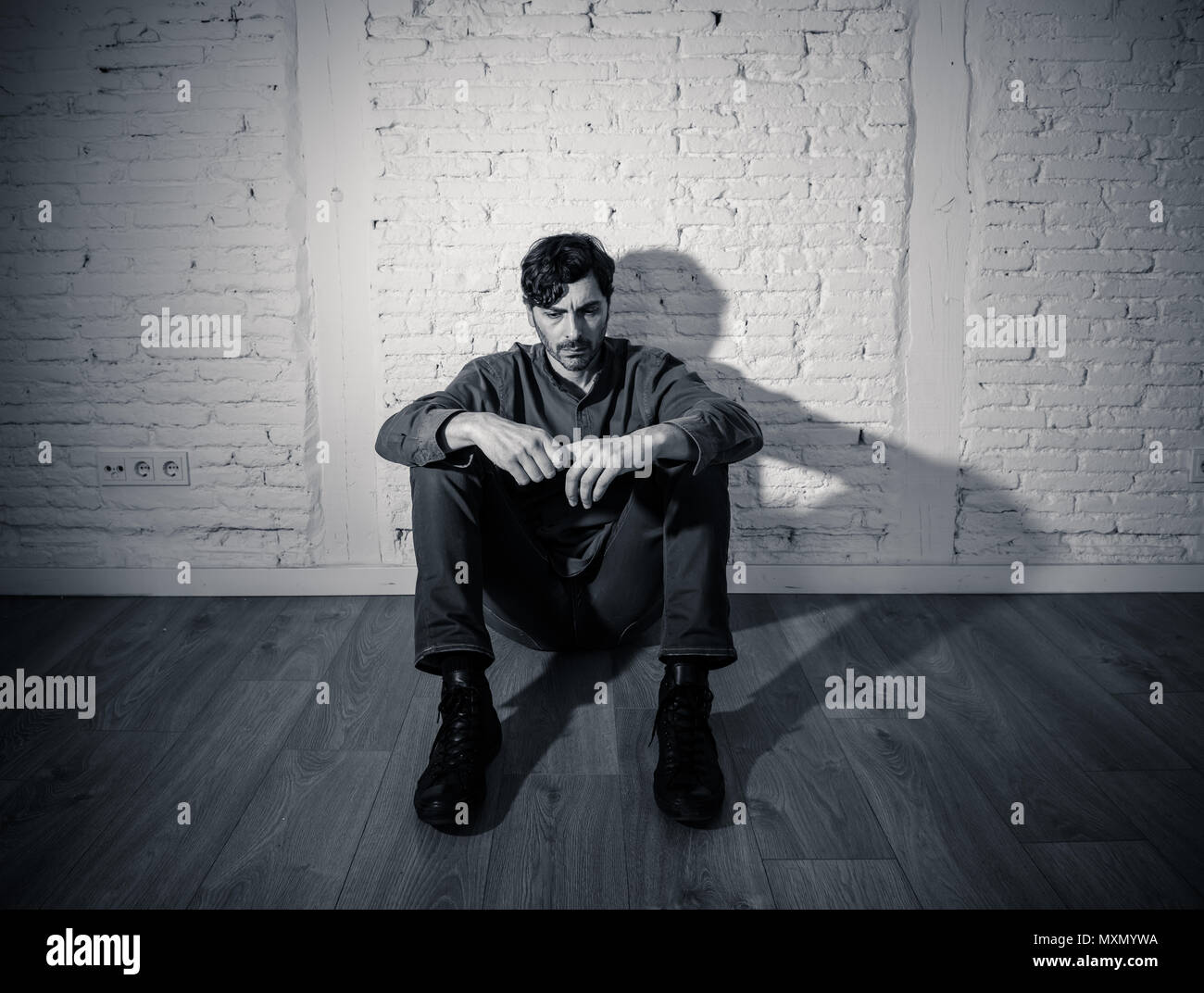young depressed man sitting against a white wall at home with a shadow ...