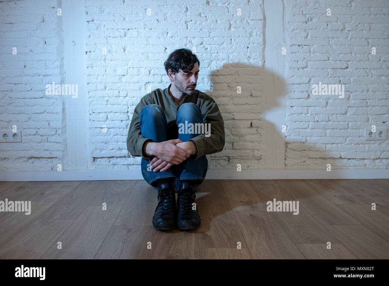 young depressed man sitting against a white wall at home with a shadow ...