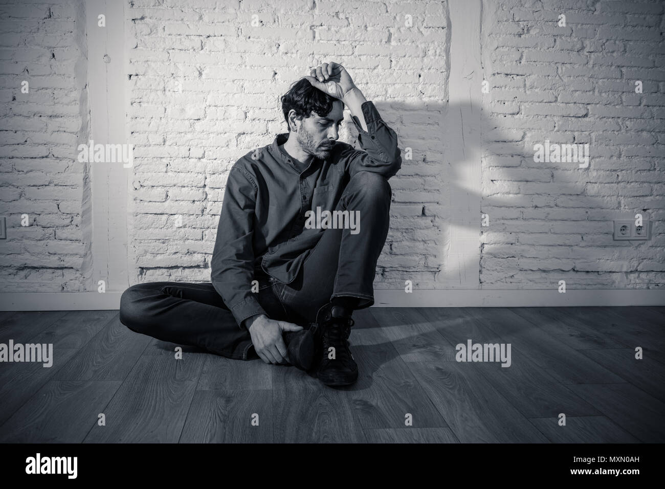 young depressed man sitting against a white wall at home with a shadow ...