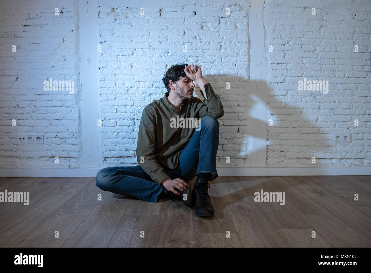 young depressed man sitting against a white wall at home with a shadow ...