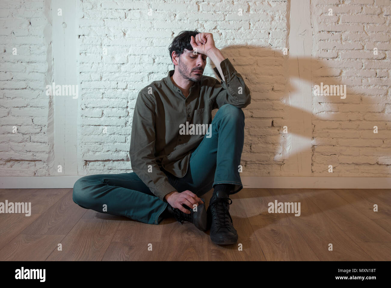 young depressed man sitting against a white wall at home with a shadow ...