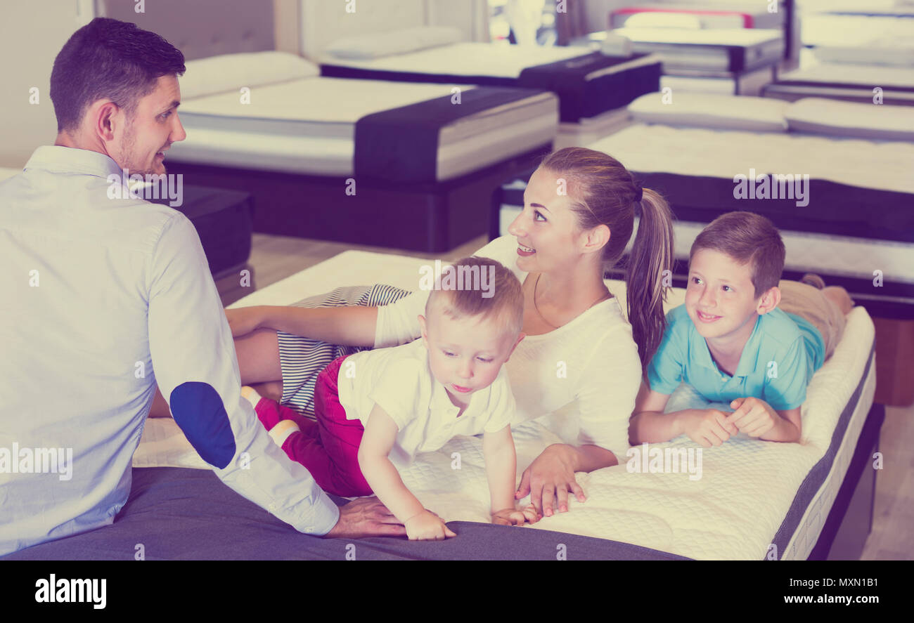 Happy parents with two sons testing mattress in store, looking at each ...