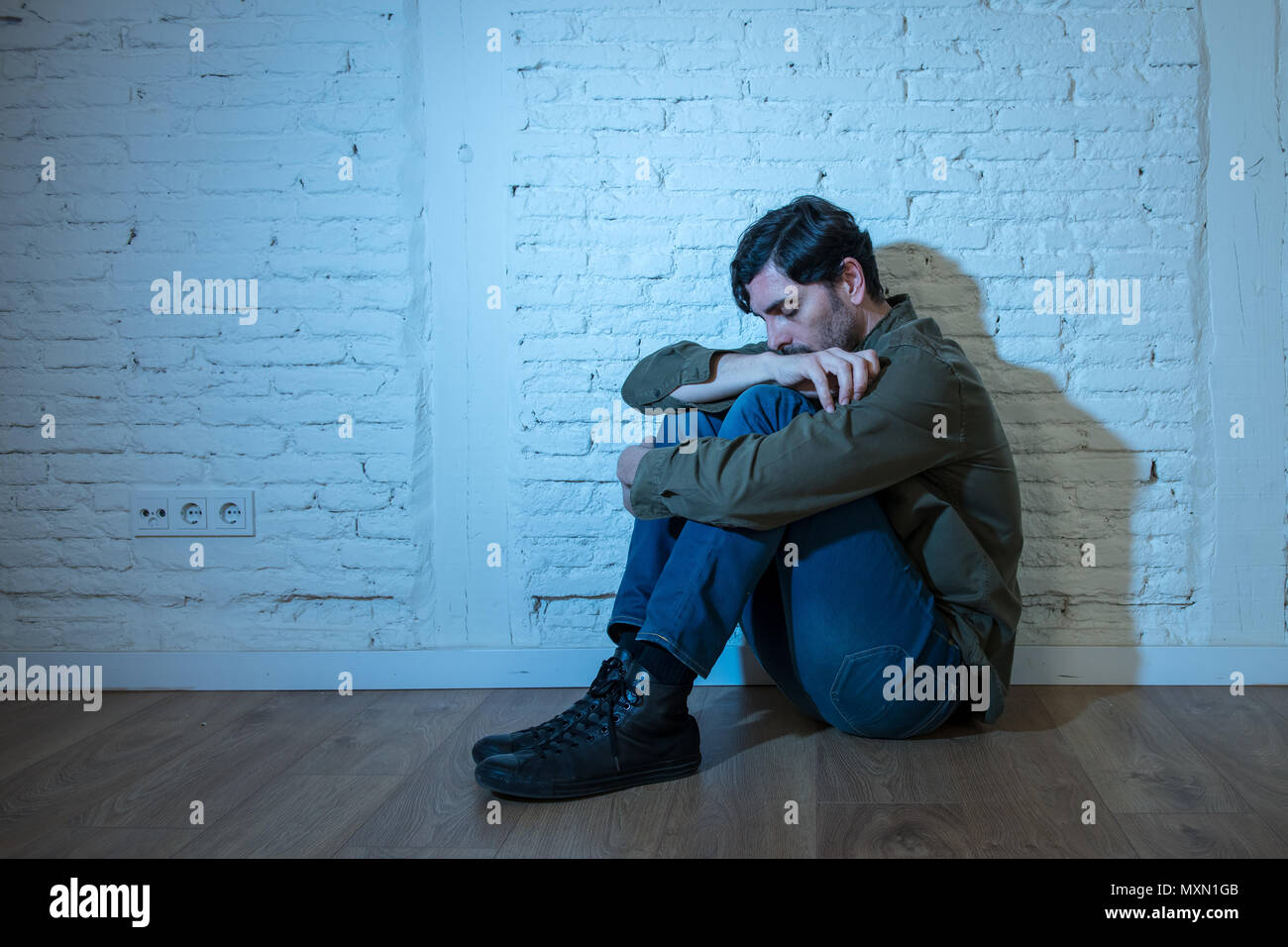 young depressed man sitting against a white wall at home with a shadow ...