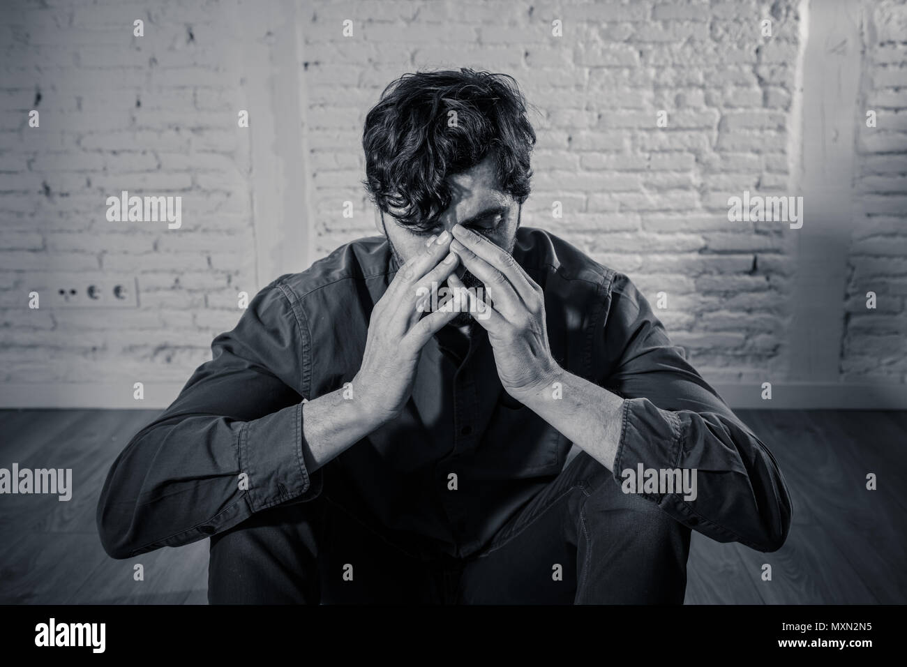 young depressed man sitting against a white wall at home with a shadow ...