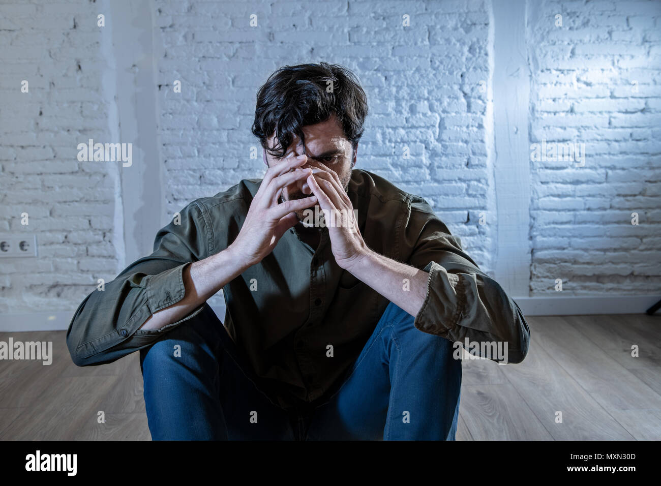young depressed man sitting against a white wall at home with a shadow ...