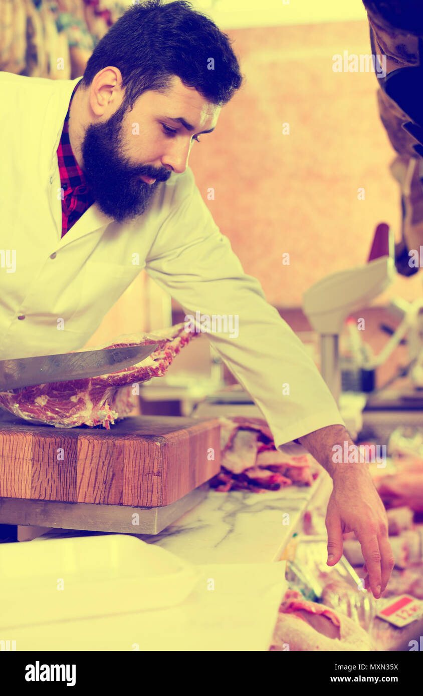 Cheerful young male seller cutting meat to sell in butcher’s shop Stock ...