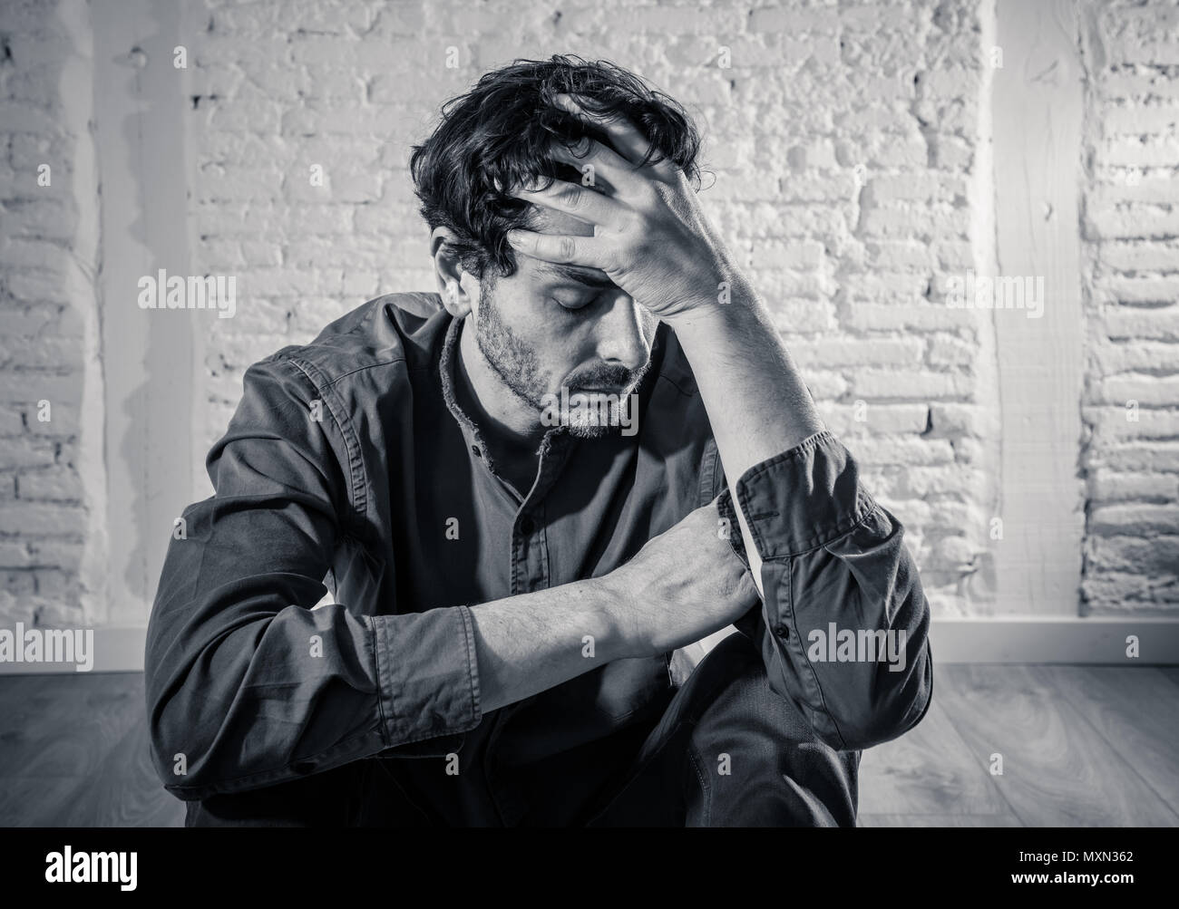 young depressed man sitting against a white wall at home with a shadow ...