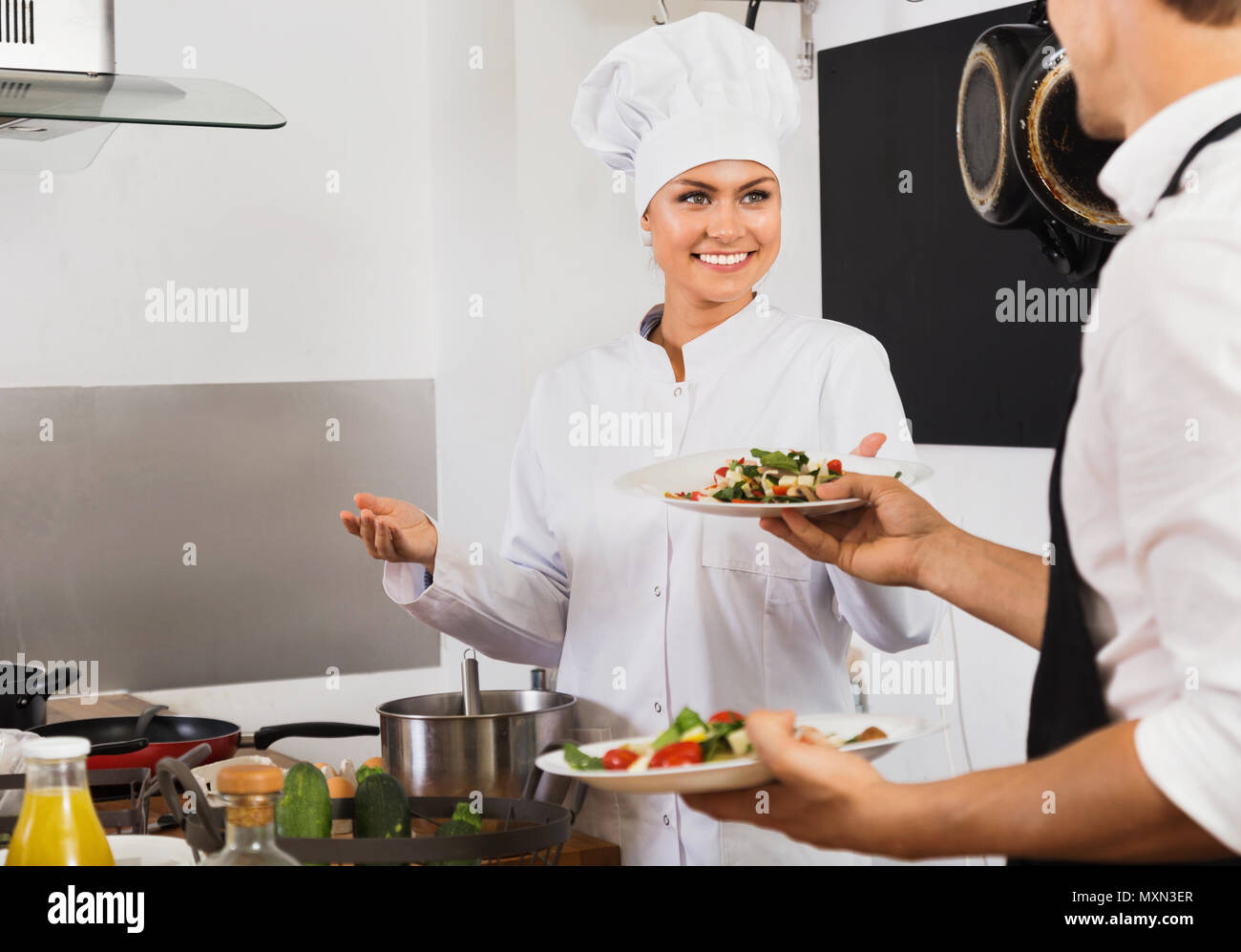 Portrait of diligent smiling woman cook giving to waitress ready to ...