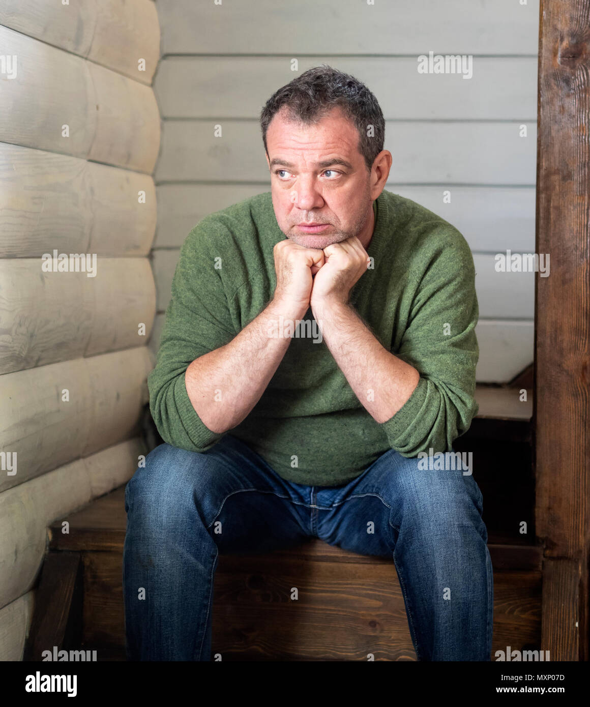 Sad Caucasian middle-aged man sitting on the stairs inside the house ...