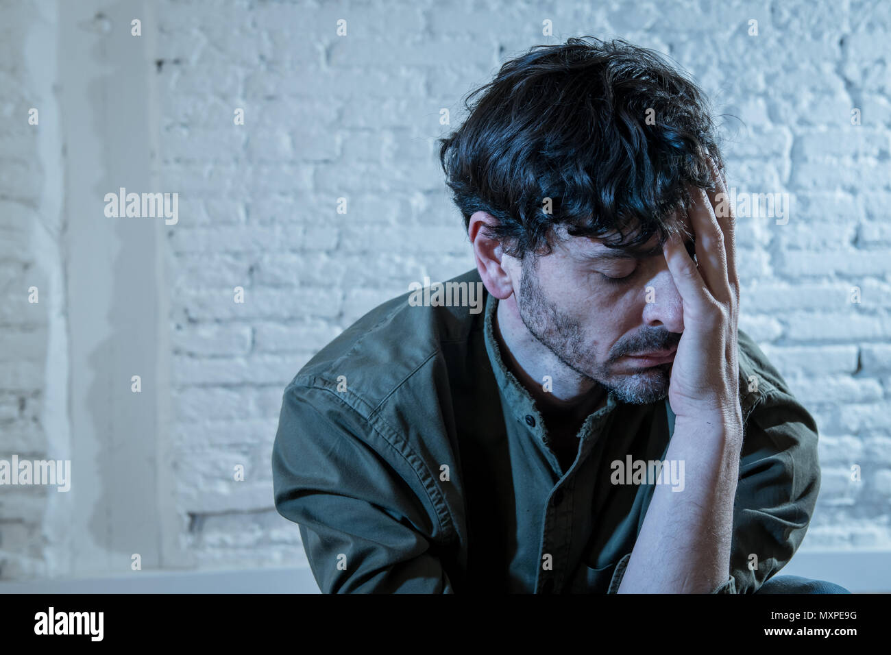 young depressed man sitting against a white wall at home with a shadow ...