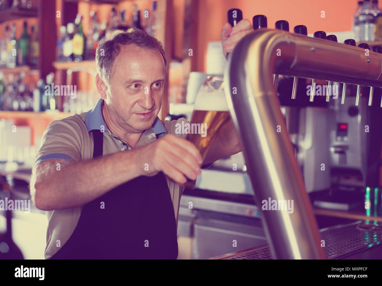 Happy cheerful positive barman is pouring unbottled beer with foam for ...