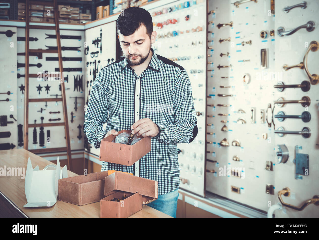 happy male seller sorting boxes with door handles in houseware shop ...