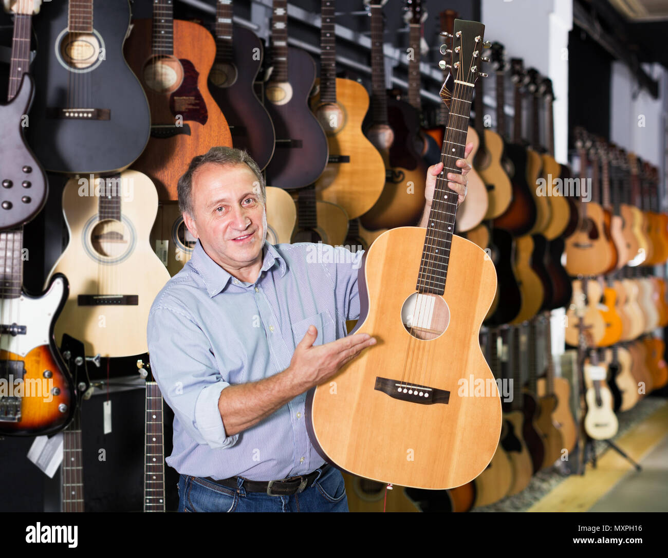 Smiling guitarist is holding modern acoustic guitar in music store ...