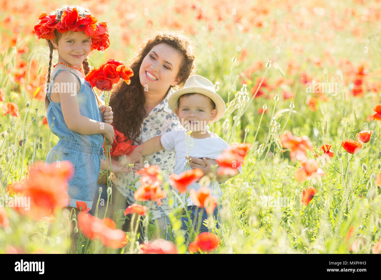 Smiling brunette in a poppy field with her family. Mom and her kids on ...