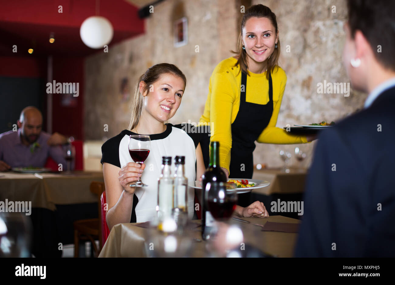 Polite waitress bringing ordered dishes to positive couple at ...