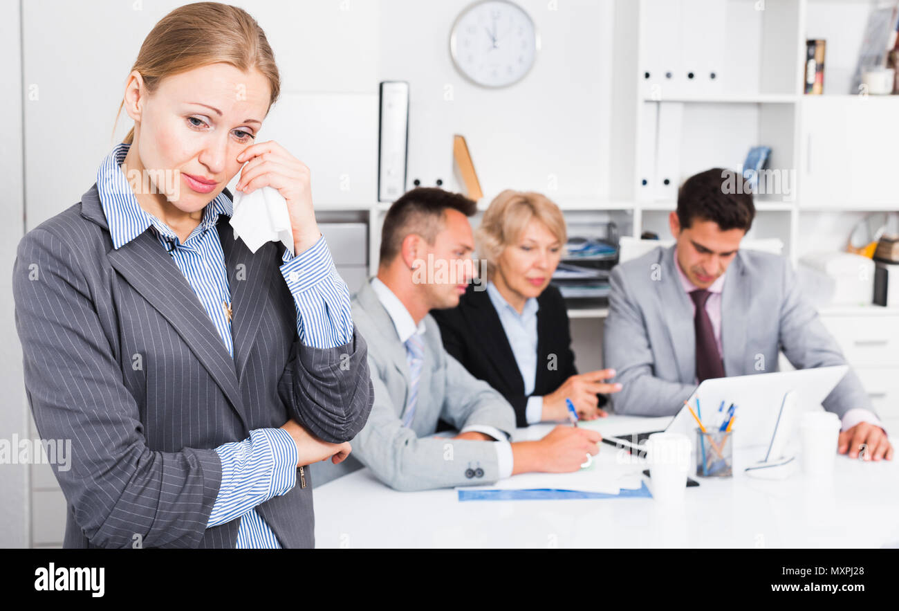 Business woman crying standing in office with working colleagues behind ...