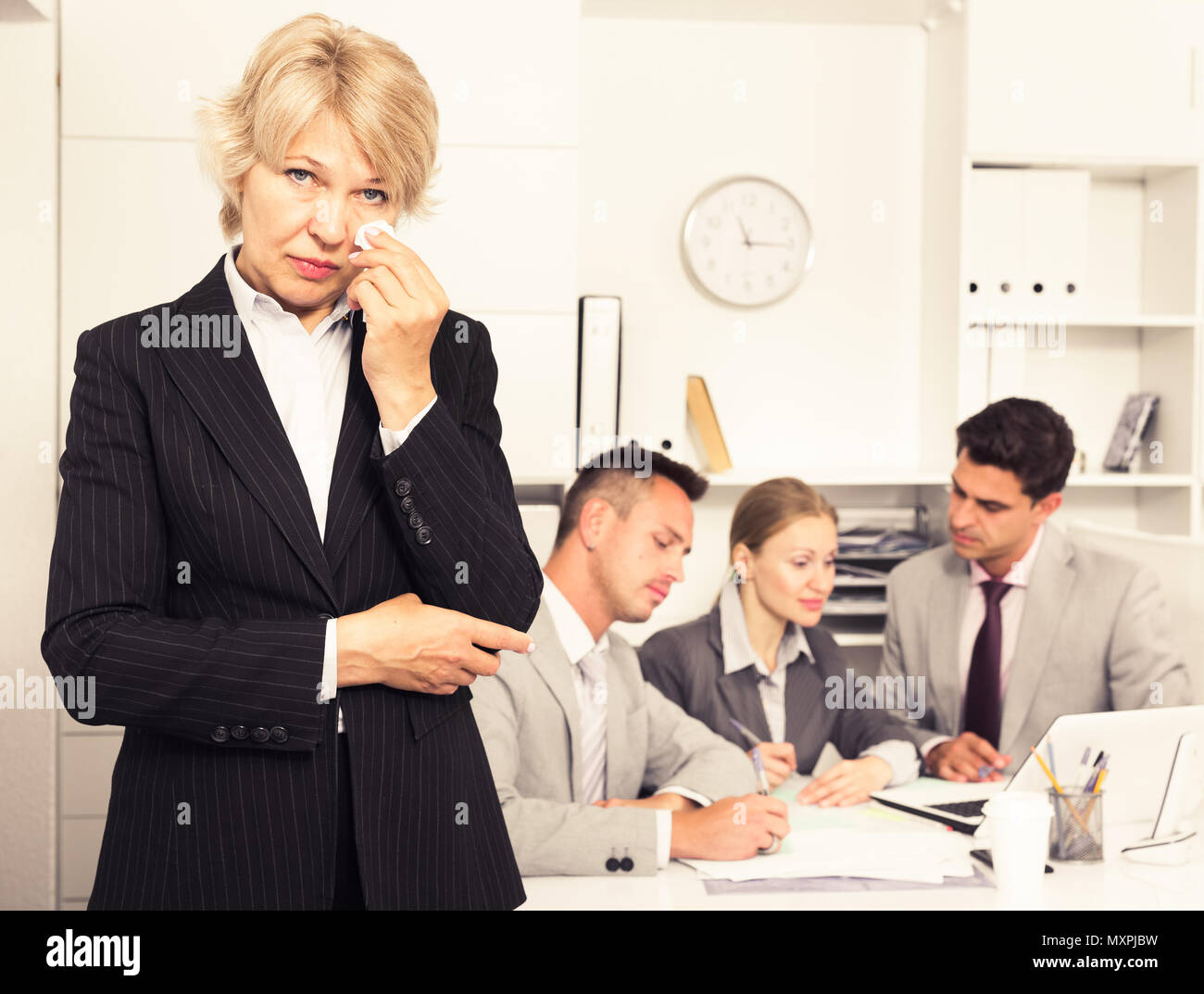 Business woman crying standing in office with working colleagues behind ...