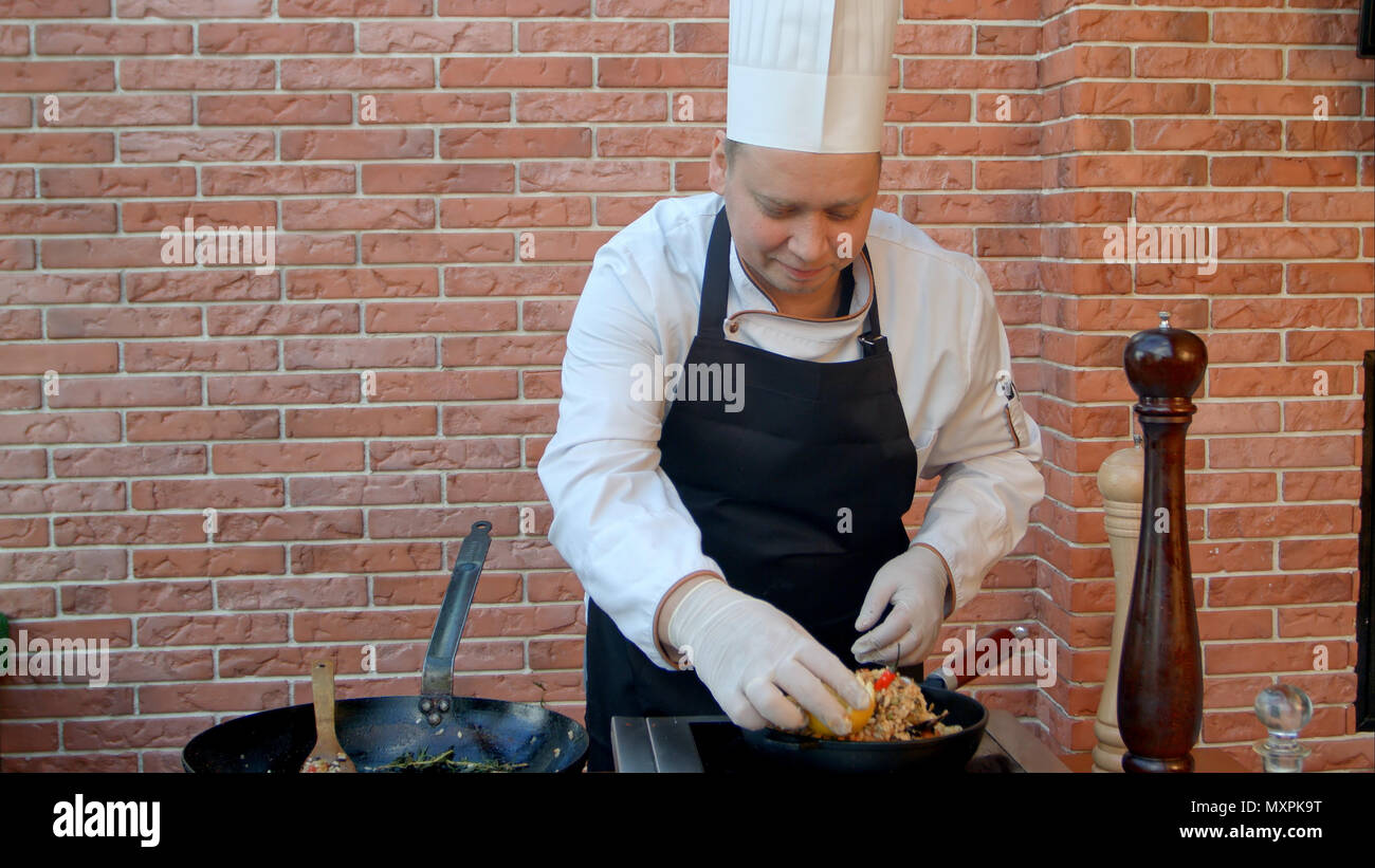 Handsome male chef dressed in white uniform decorating paella and ...