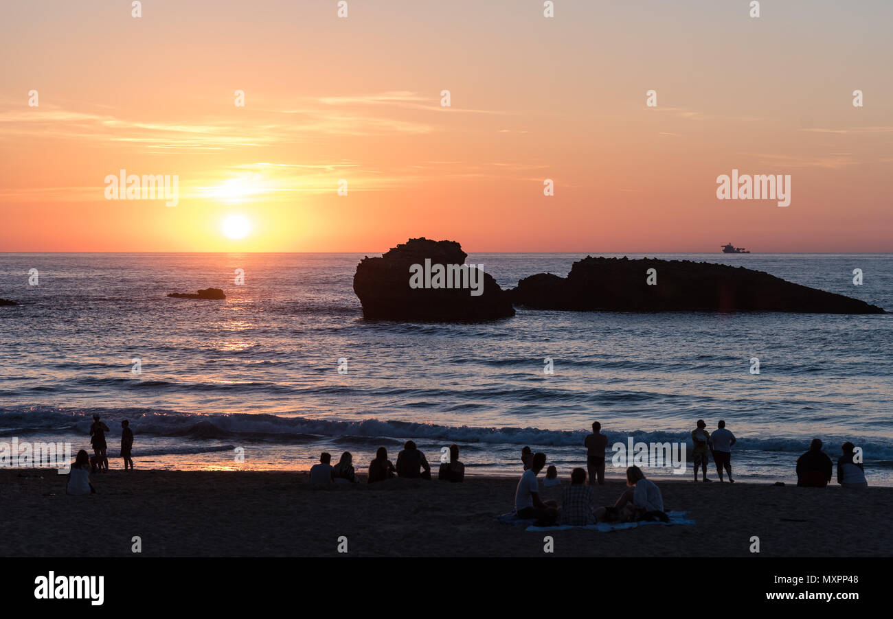 Sun setting in the horizon over the ocean with people watching Stock ...