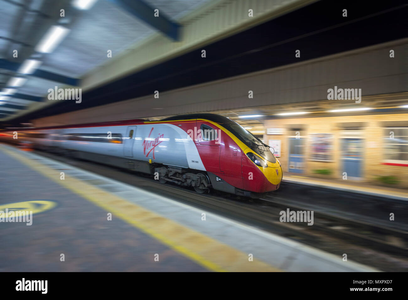 Virgin Pendolino train at speed passing through a station at night ...
