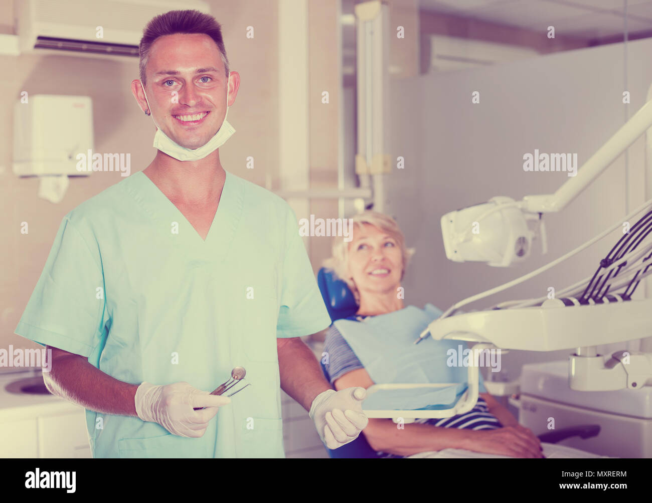 Confident male dentist standing in dental office with female patient in ...