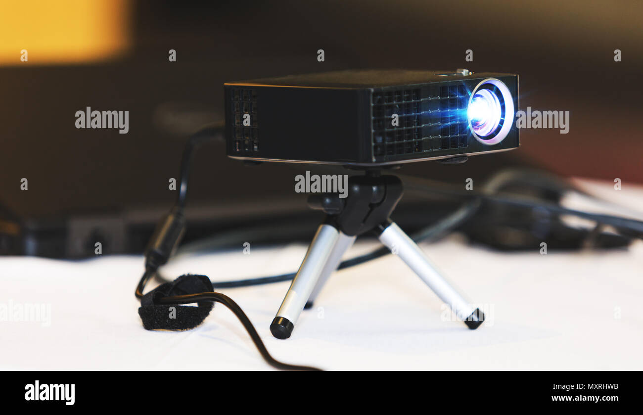 Black projector with tripod installed on white table, in hall or ...