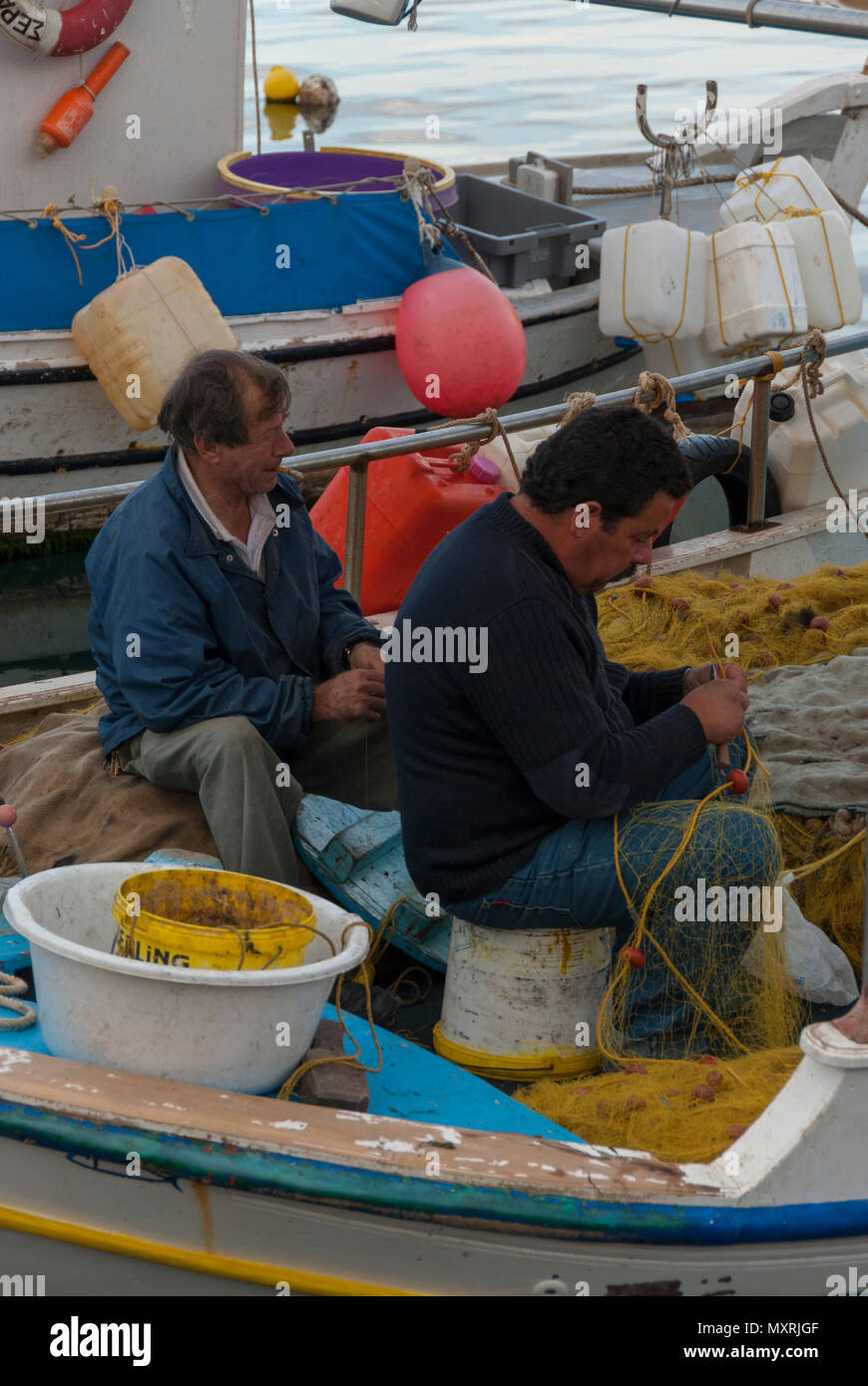 Cretan fishermen mending their nets on a colourful fishing boat in the ...