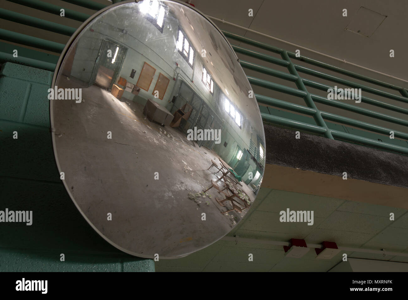 Security mirror reflecting common area and library cage in old prison ...