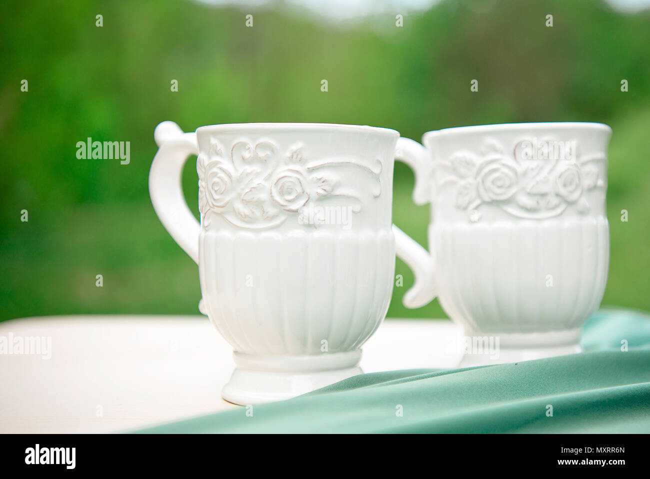 two white empty cups on table against green background outdoor Stock ...